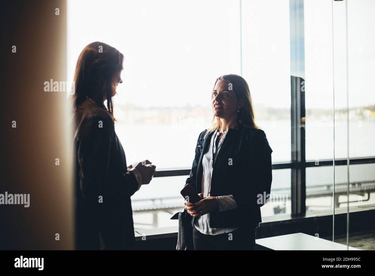 Female colleagues discussing while standing at workplace Stock Photo ...
