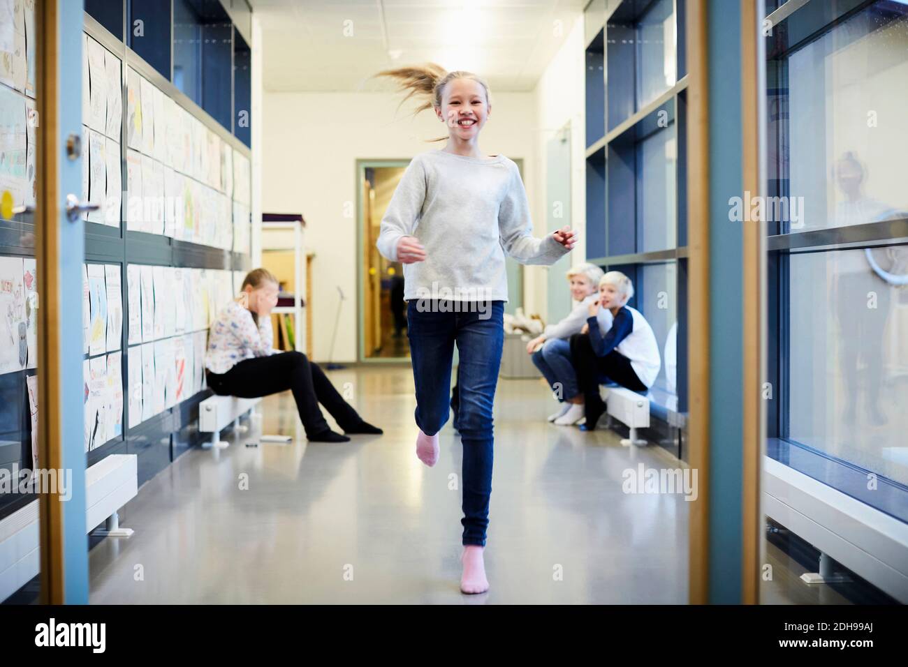 Smiling girl running in school corridor with friends in background ...
