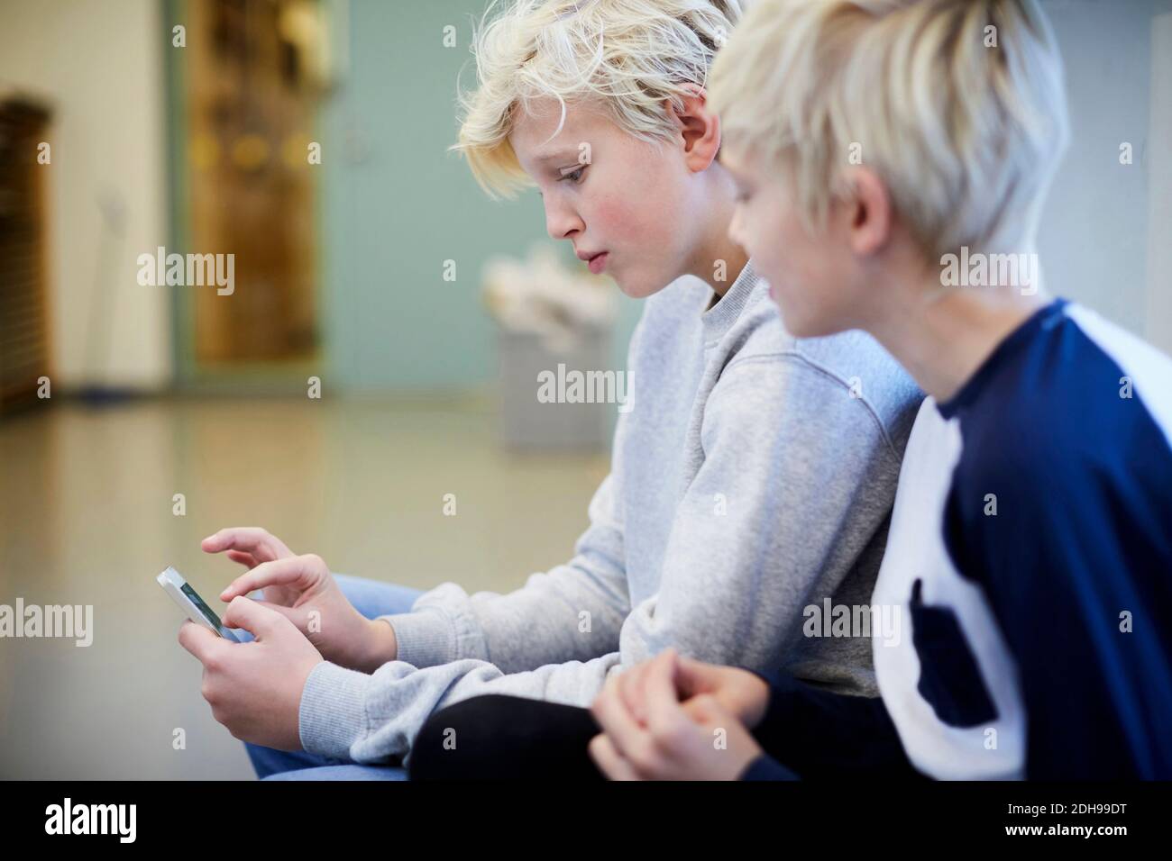 Boy looking at friend using mobile phone in school corridor Stock Photo ...