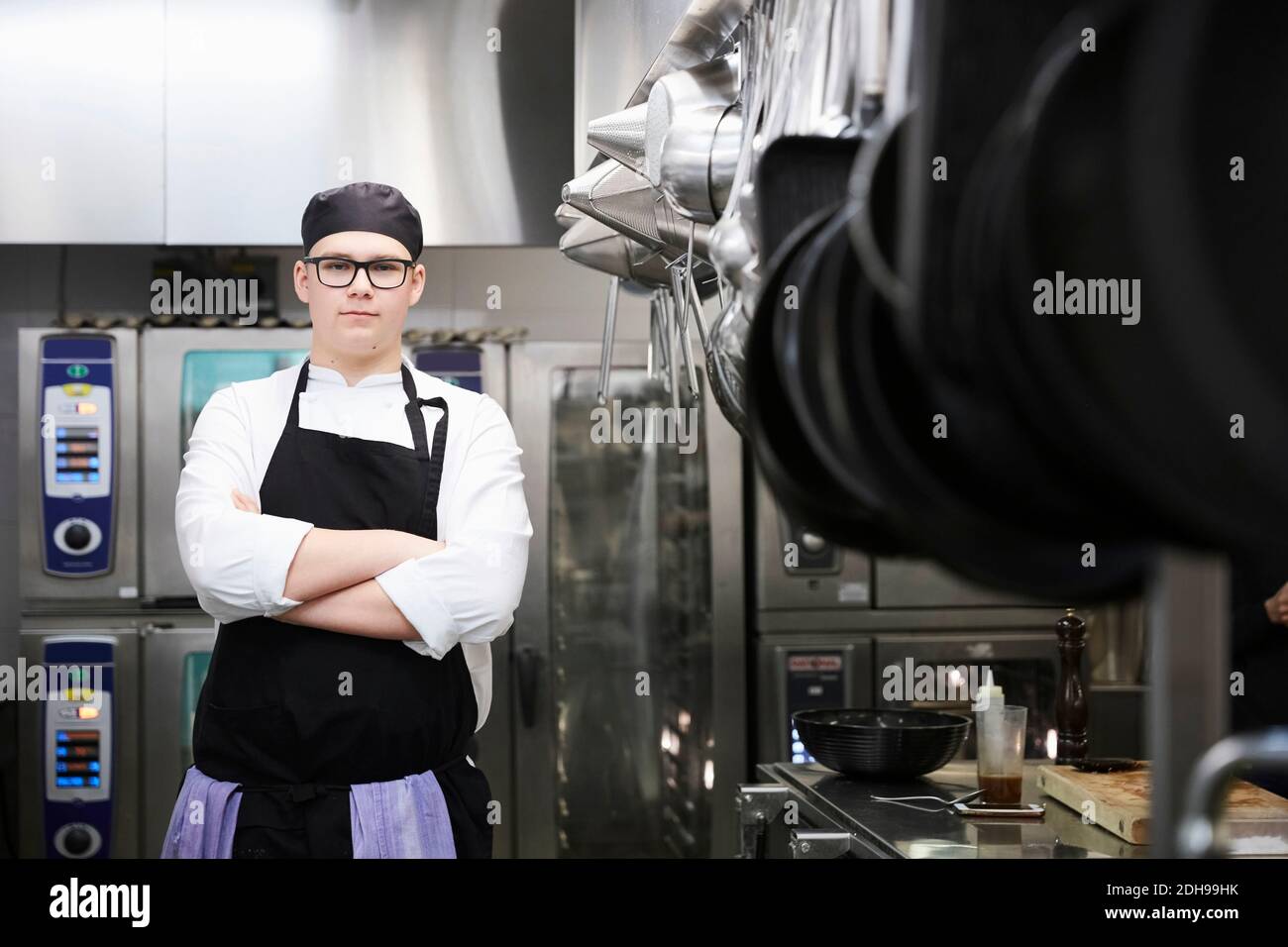 Portrait of male chef student standing arms crossed in commercial ...