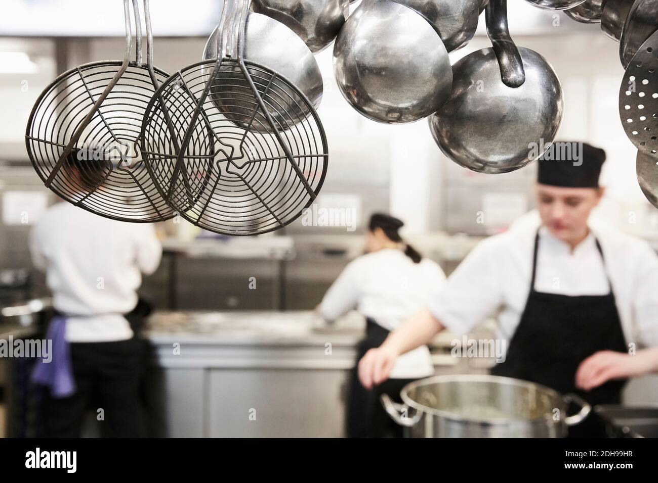 Kitchen utensils with chefs cooking in background at commercial kitchen ...