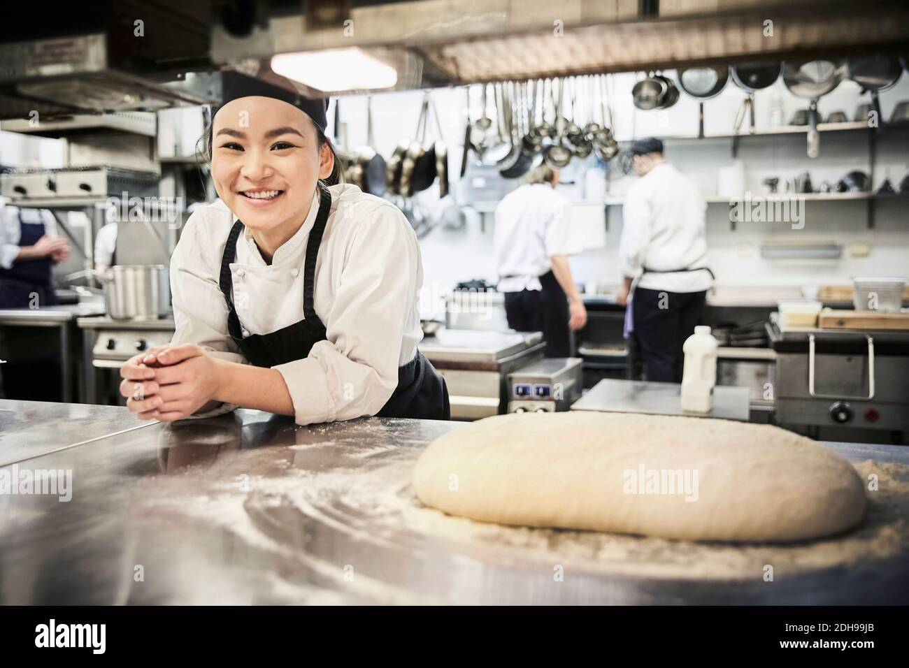 Portrait of smiling female chef leaning on counter in commercial ...