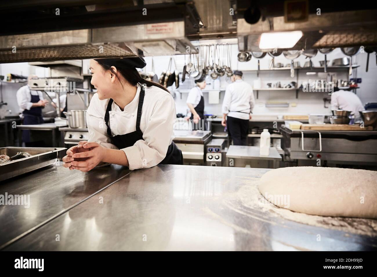 Female chef leaning on counter with colleagues in background at ...
