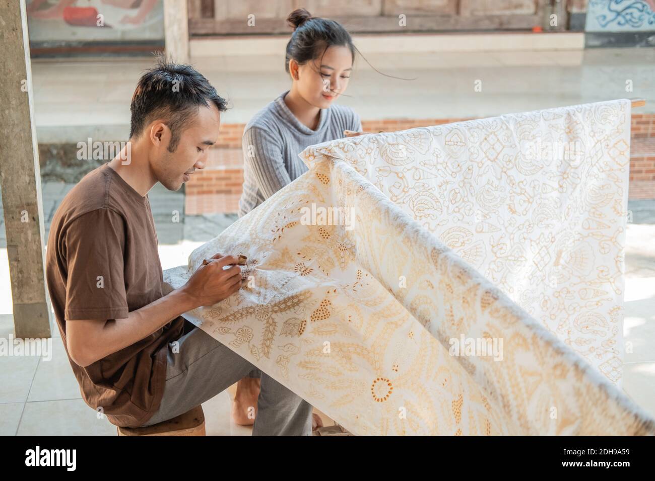 young woman and man drawing batik on a white cloth using canting Stock ...
