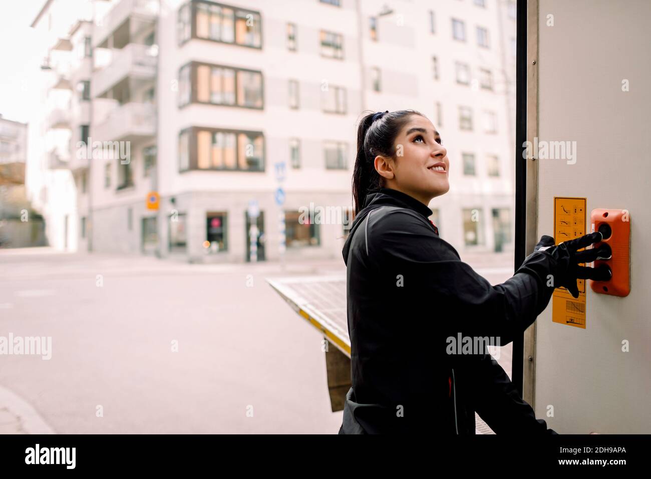 Smiling young delivery woman pressing push buttons on truck in city ...