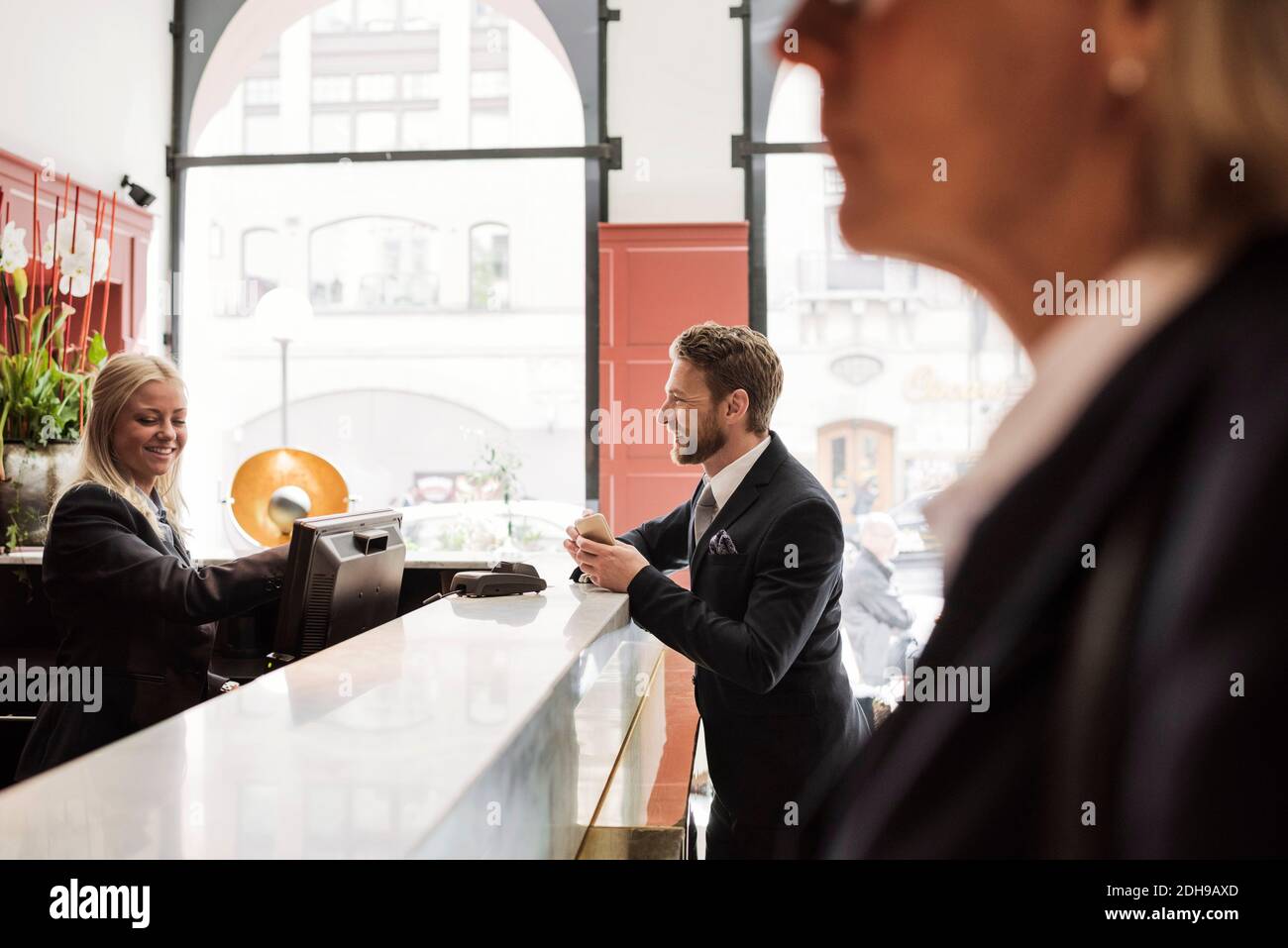 Happy businessman talking to female receptionist at hotel reception ...