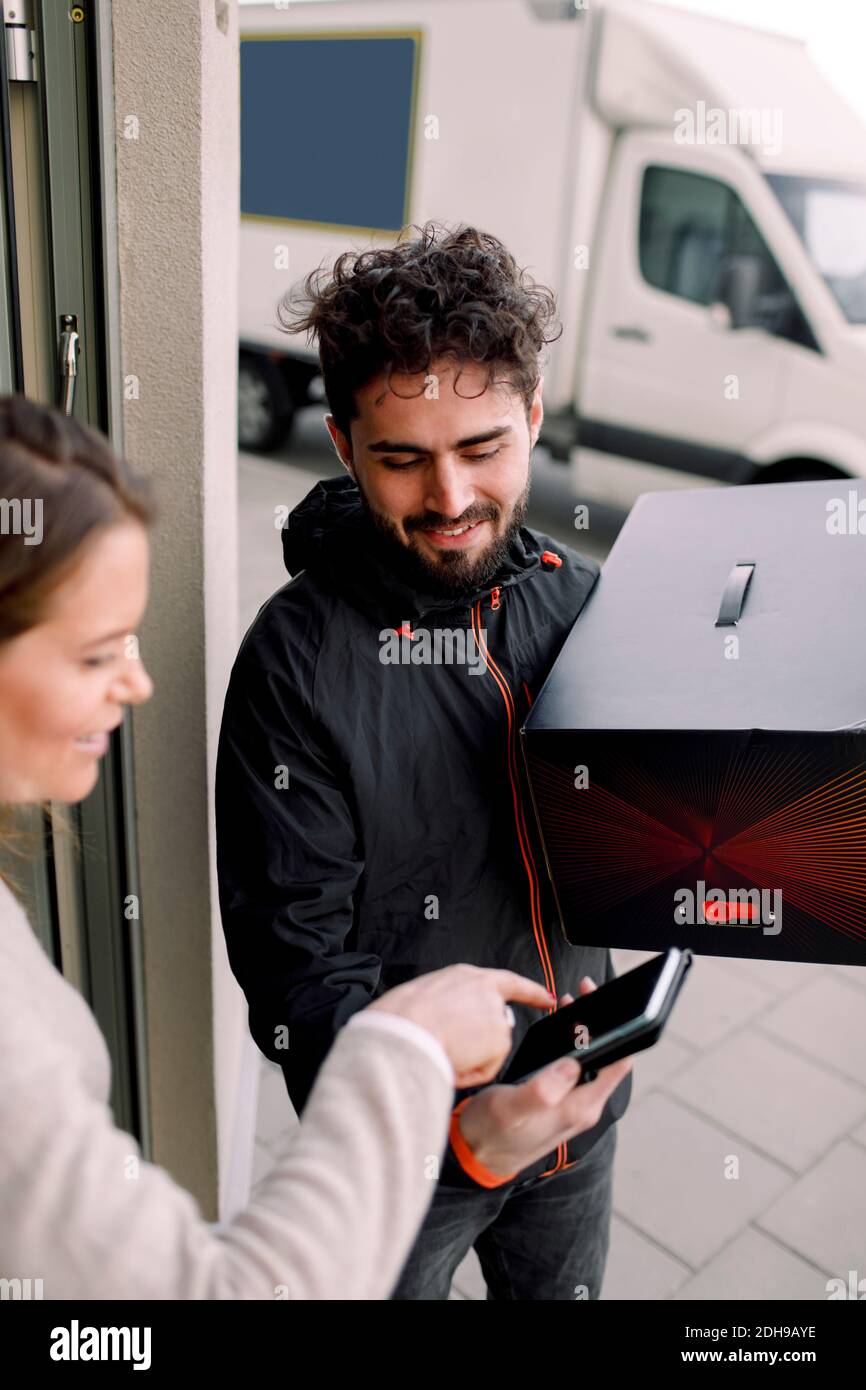 Female customer signing on smart phone while receiving box from ...