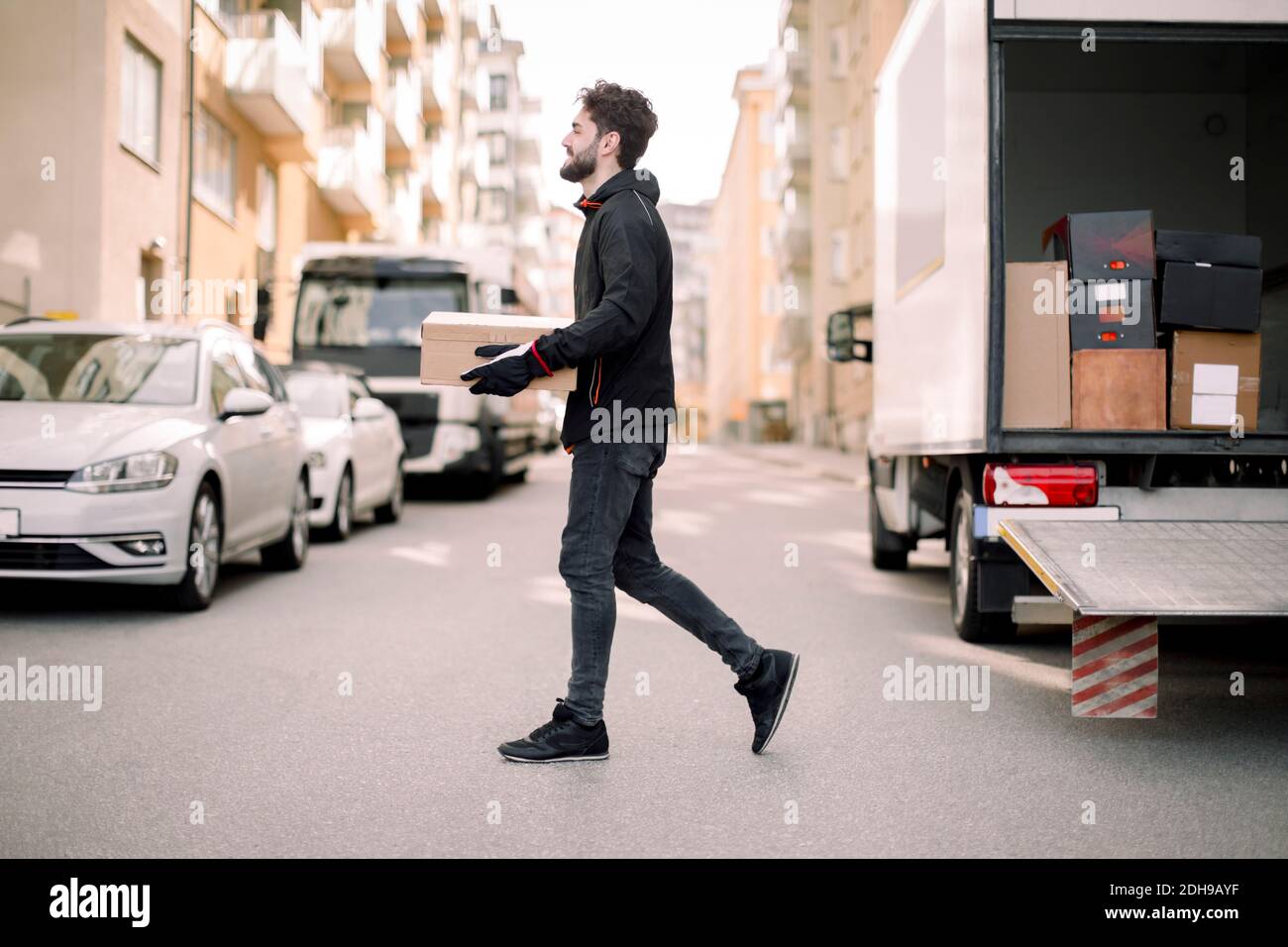 Side view of young delivery man carrying box while walking on street in ...
