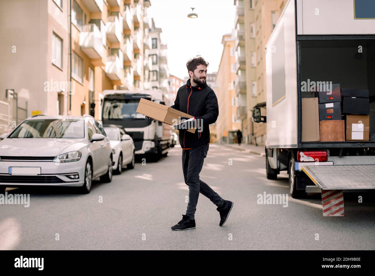 Young delivery man carrying box while walking on street in city Stock ...