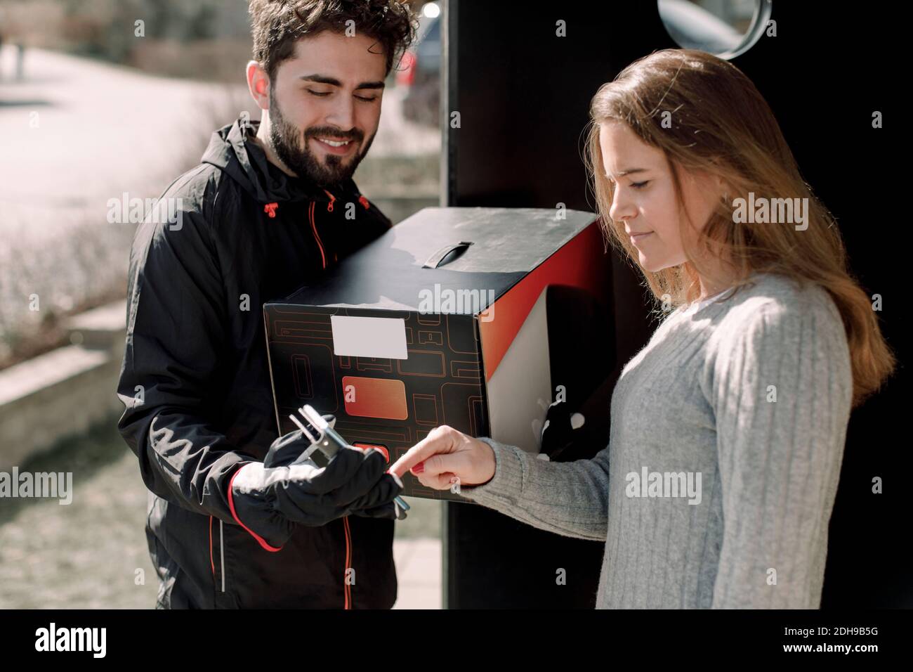 Female customer signing on mobile phone while receiving package from ...