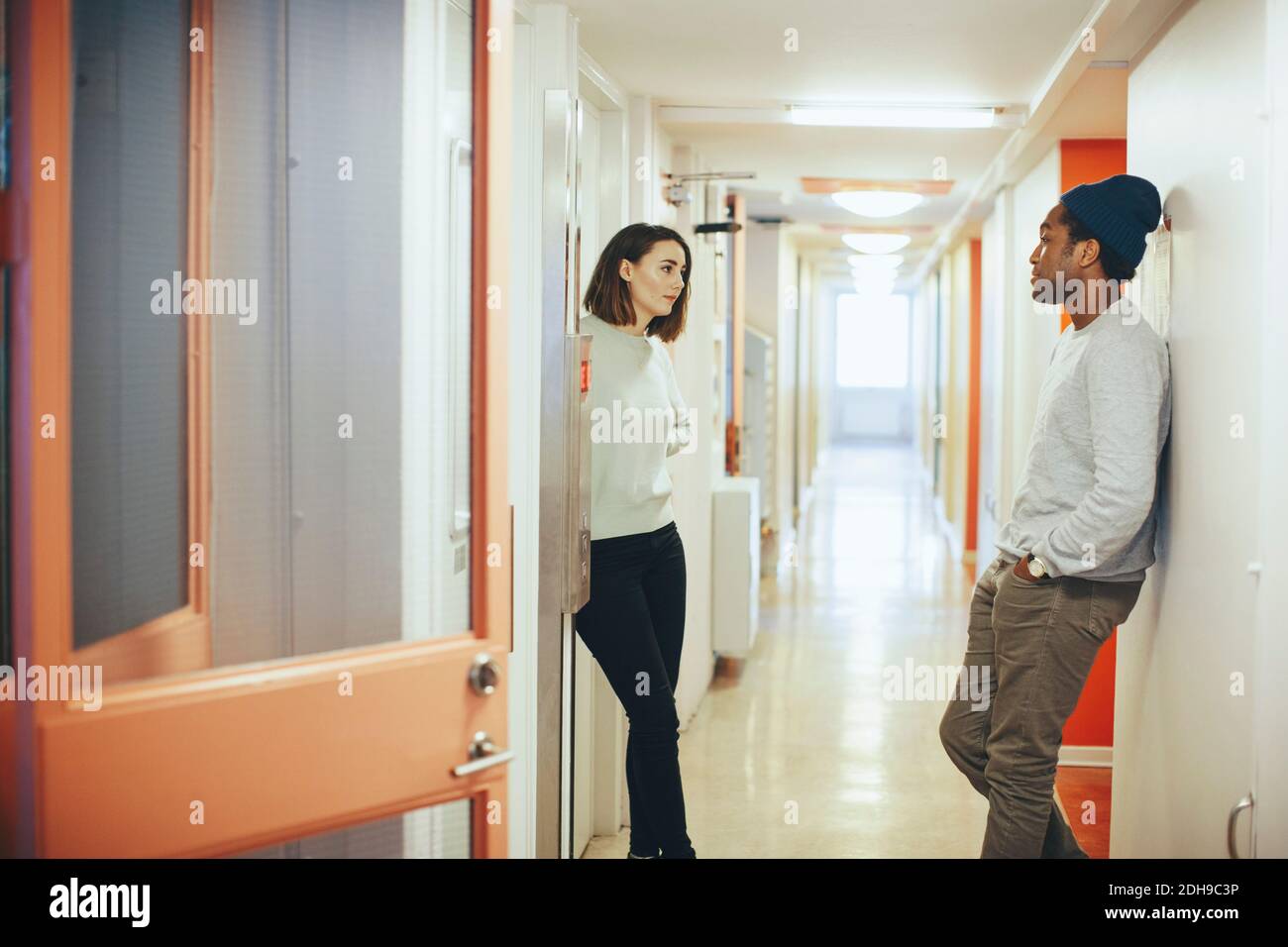 Young friends talking while standing in college dorm corridor Stock ...