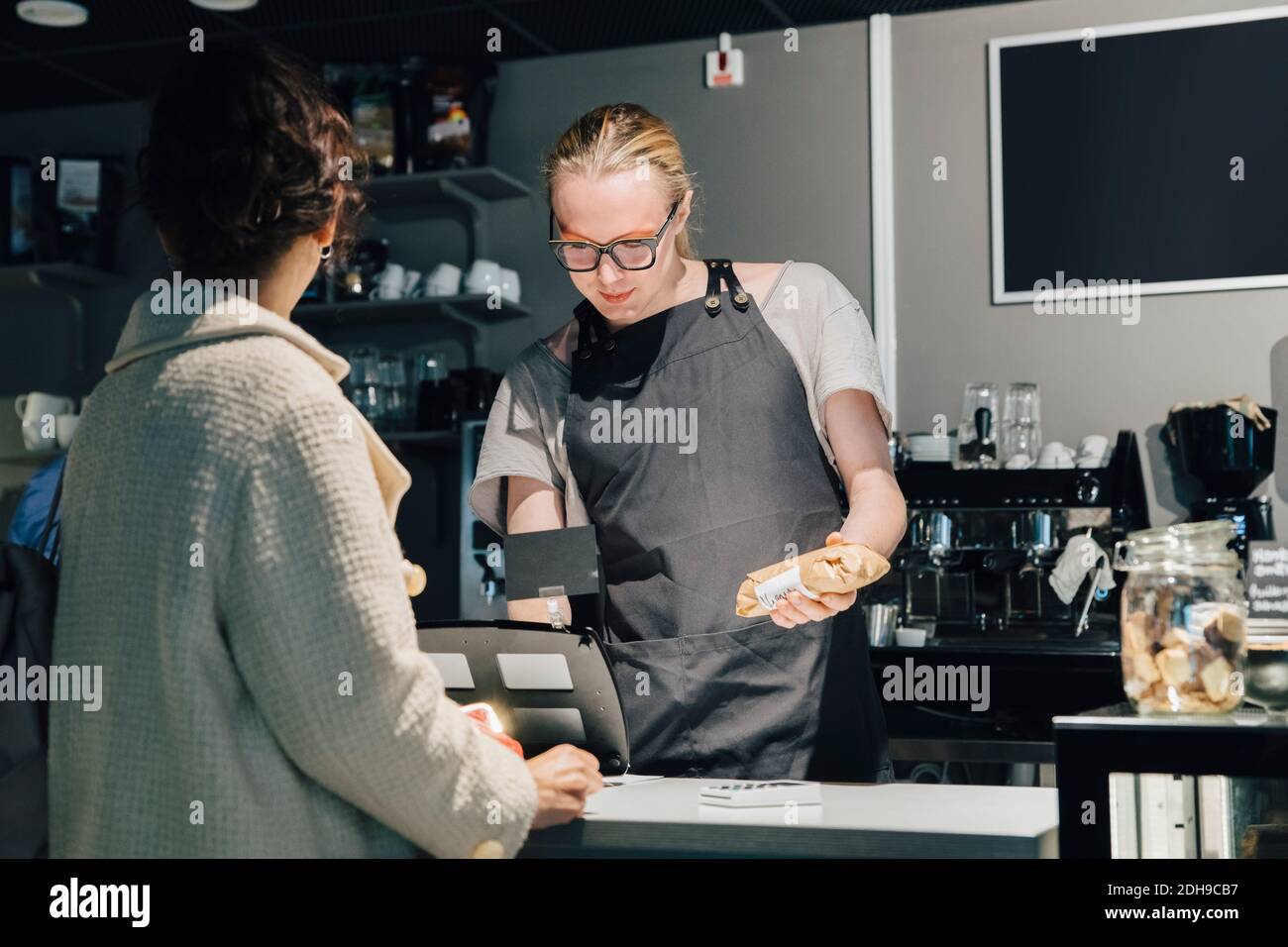 Customer standing with transgender cashier at checkout in illuminated ...