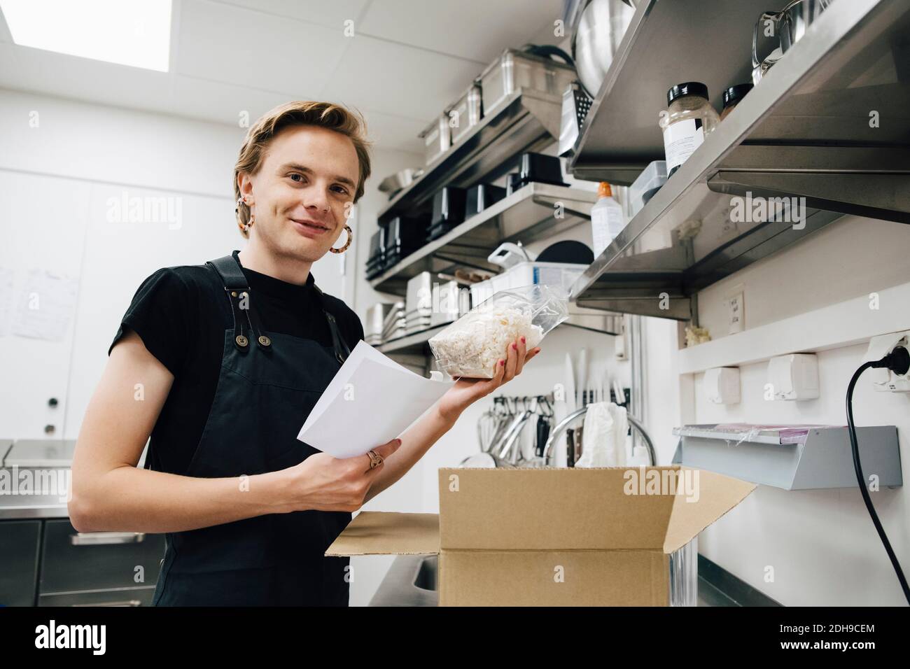 Portrait of smiling transgender owner with list and package in coffee ...