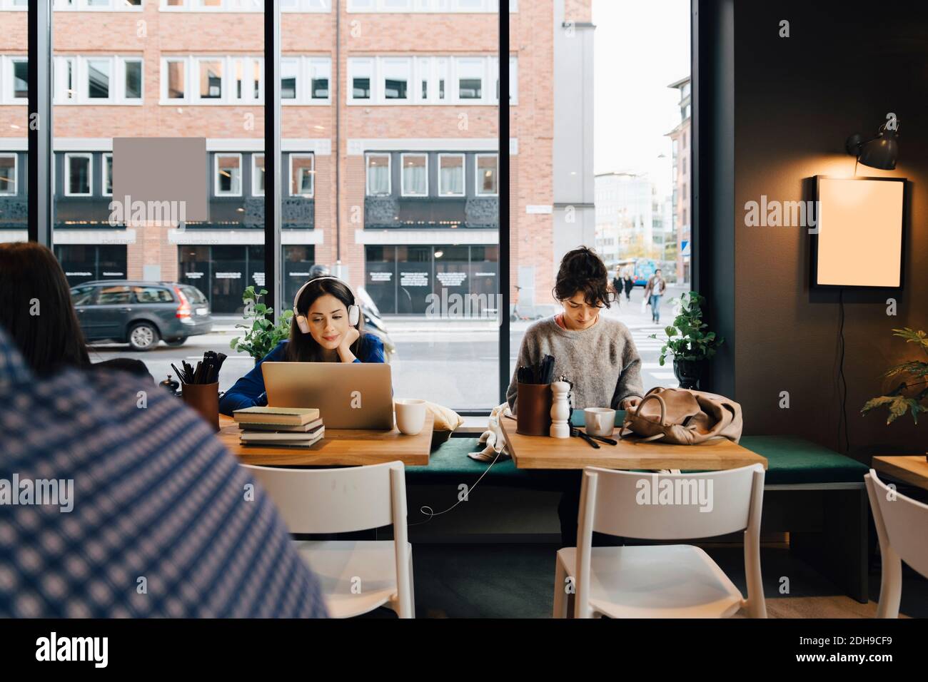 Female customers sitting at tables against window in coffee shop Stock ...