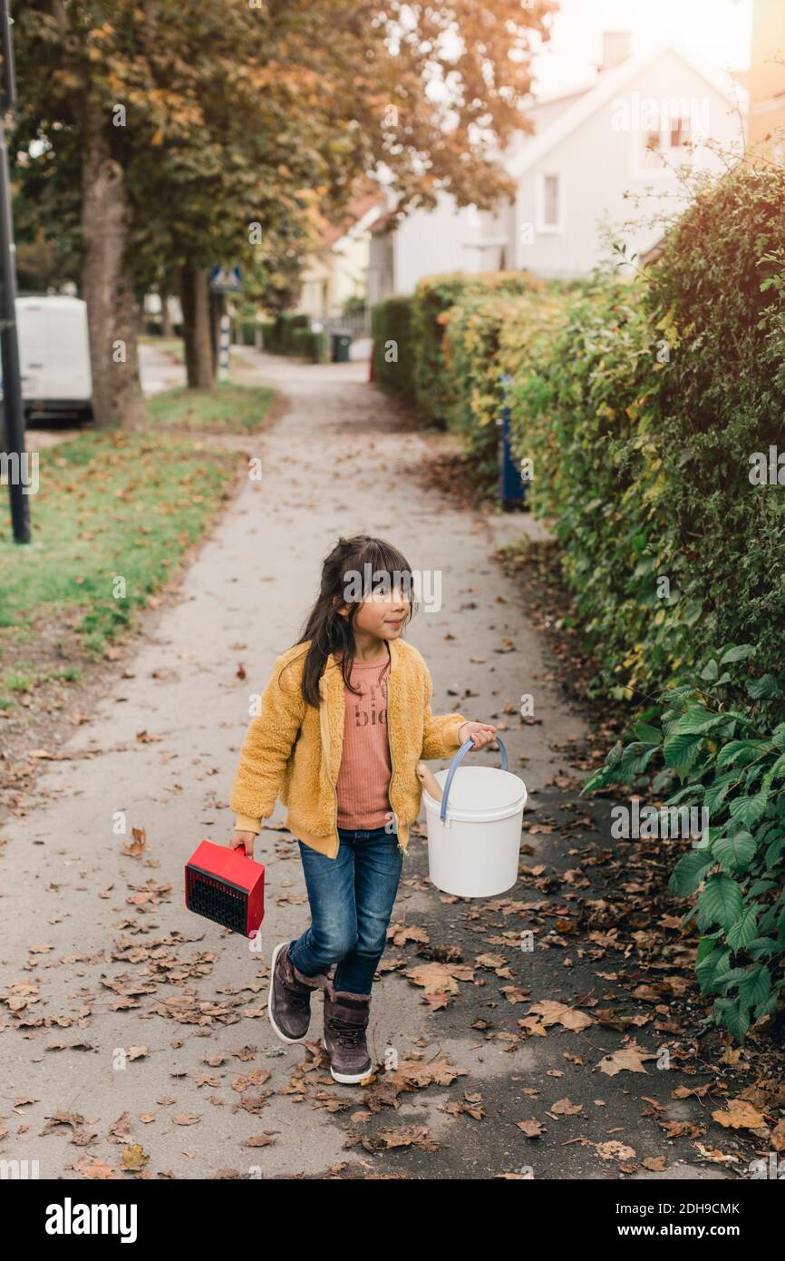 Girl carrying bucket while walking on footpath Stock Photo - Alamy