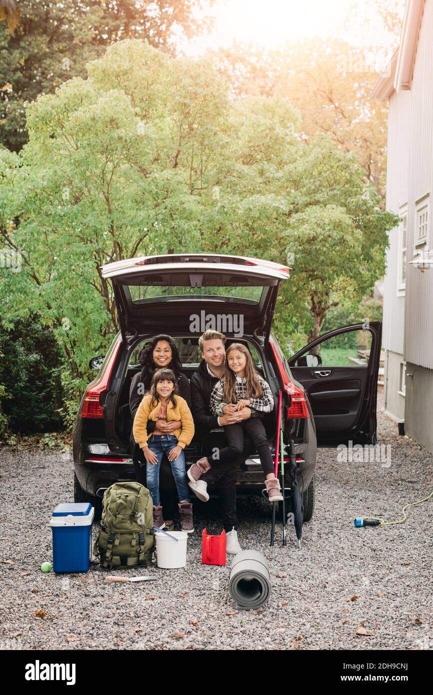 Smiling parents sitting with daughters in trunk of electric car Stock ...