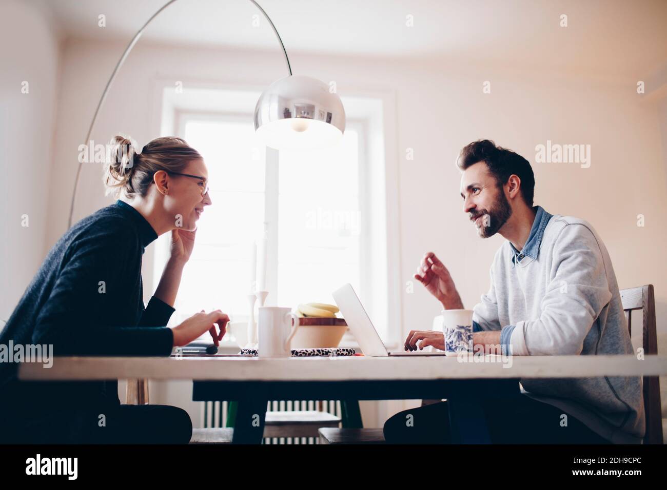 Side view of couple talking while sitting at dining table at home Stock ...