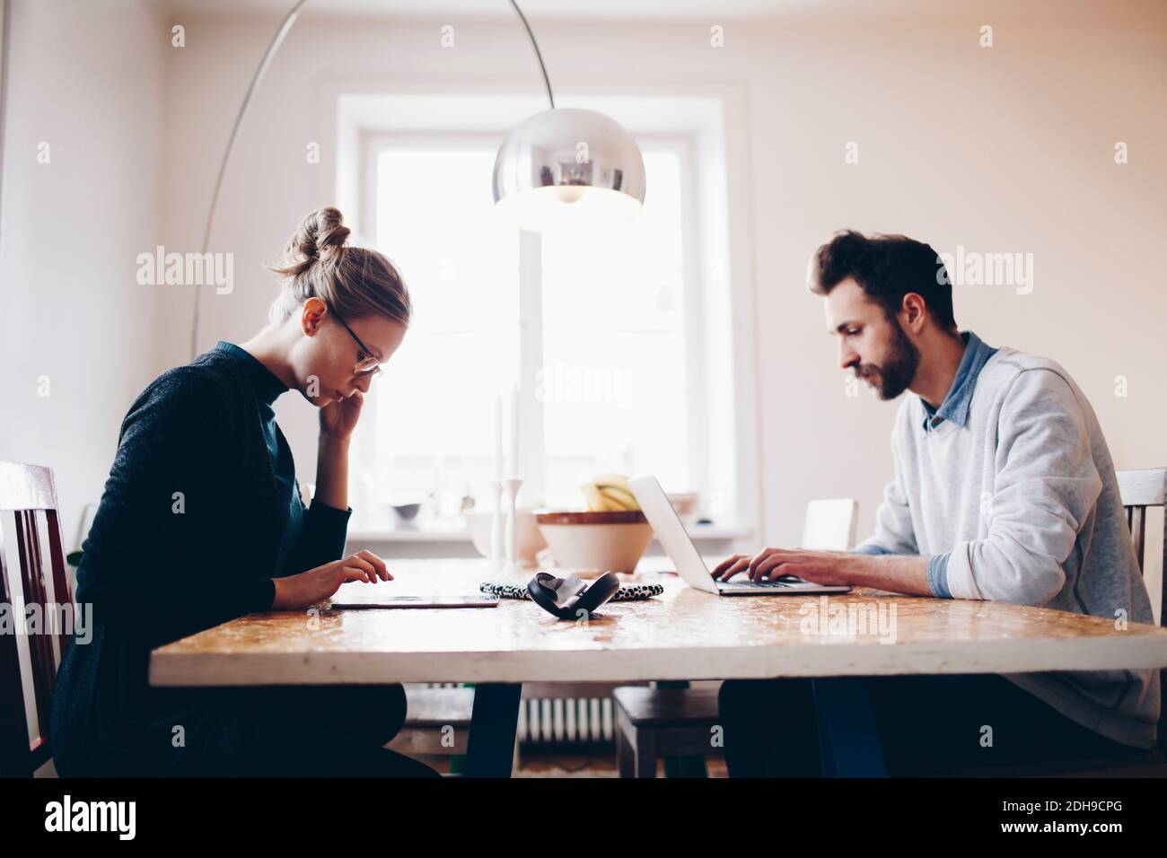 Side view of couple using technologies at dining table while working ...
