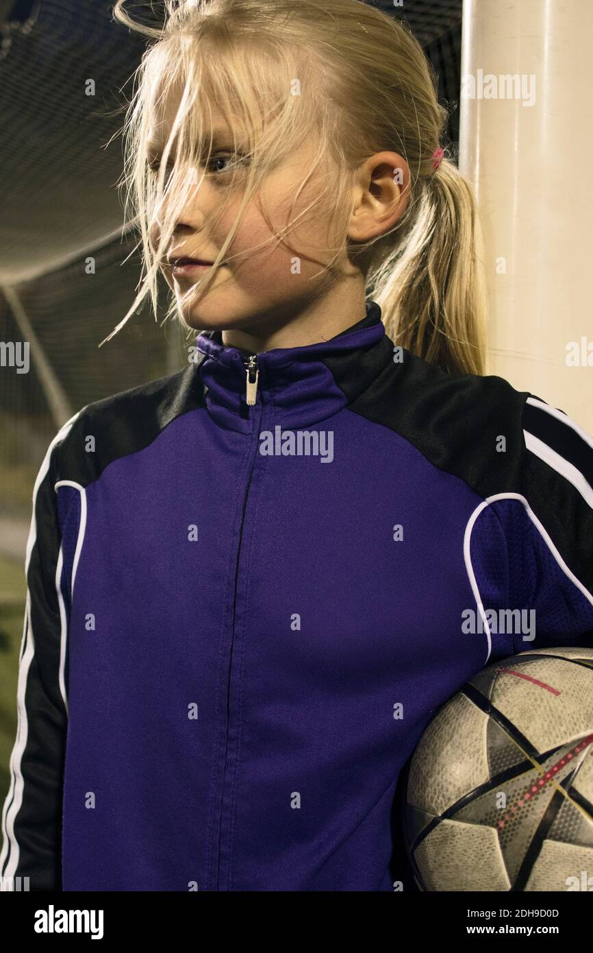 Girl holding soccer ball looking away while standing by goal post Stock ...