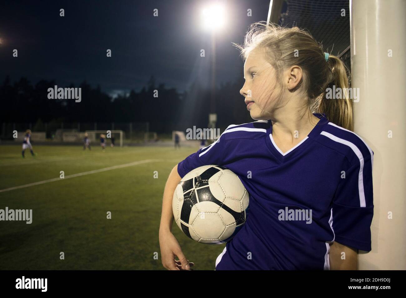 Girl holding soccer ball standing by goal post on field Stock Photo - Alamy