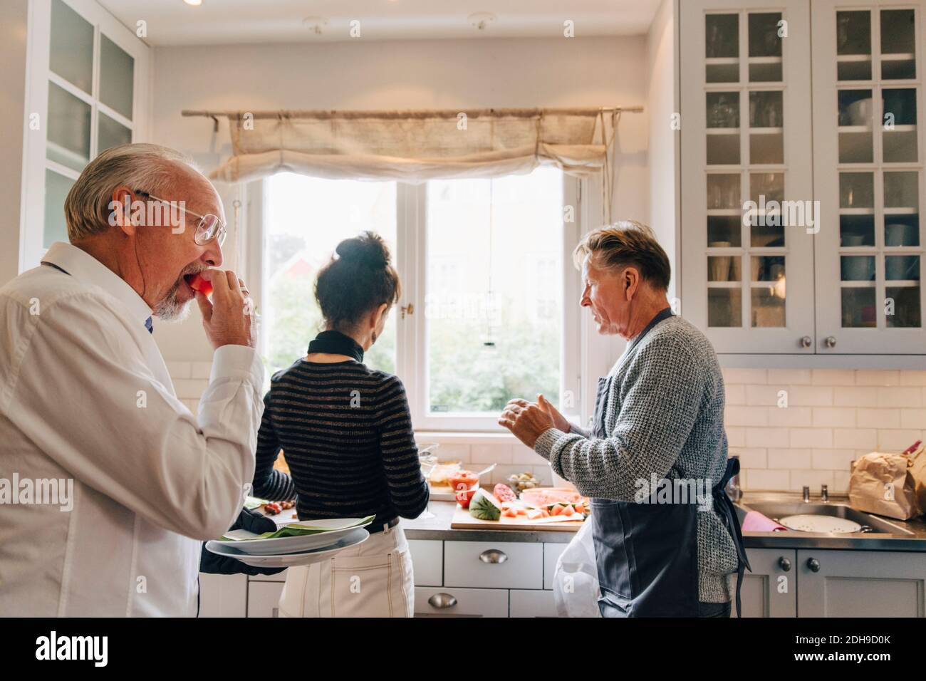 Man eating watermelon while friends talking in kitchen Stock Photo - Alamy