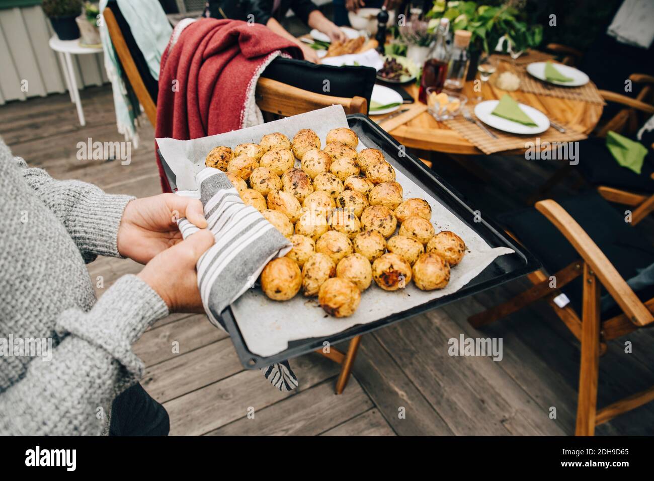 Low section of senior man holding baking sheet with baked potatoes at ...