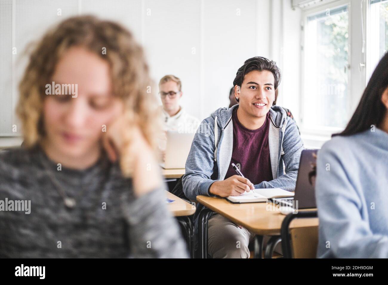 Smiling man writing in book at desk in classroom Stock Photo - Alamy