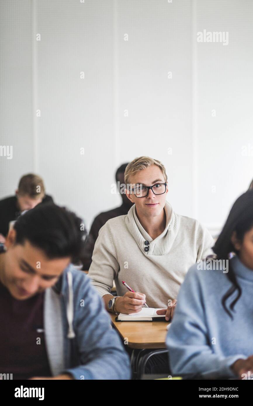 Young man writing in book at desk in classroom Stock Photo - Alamy