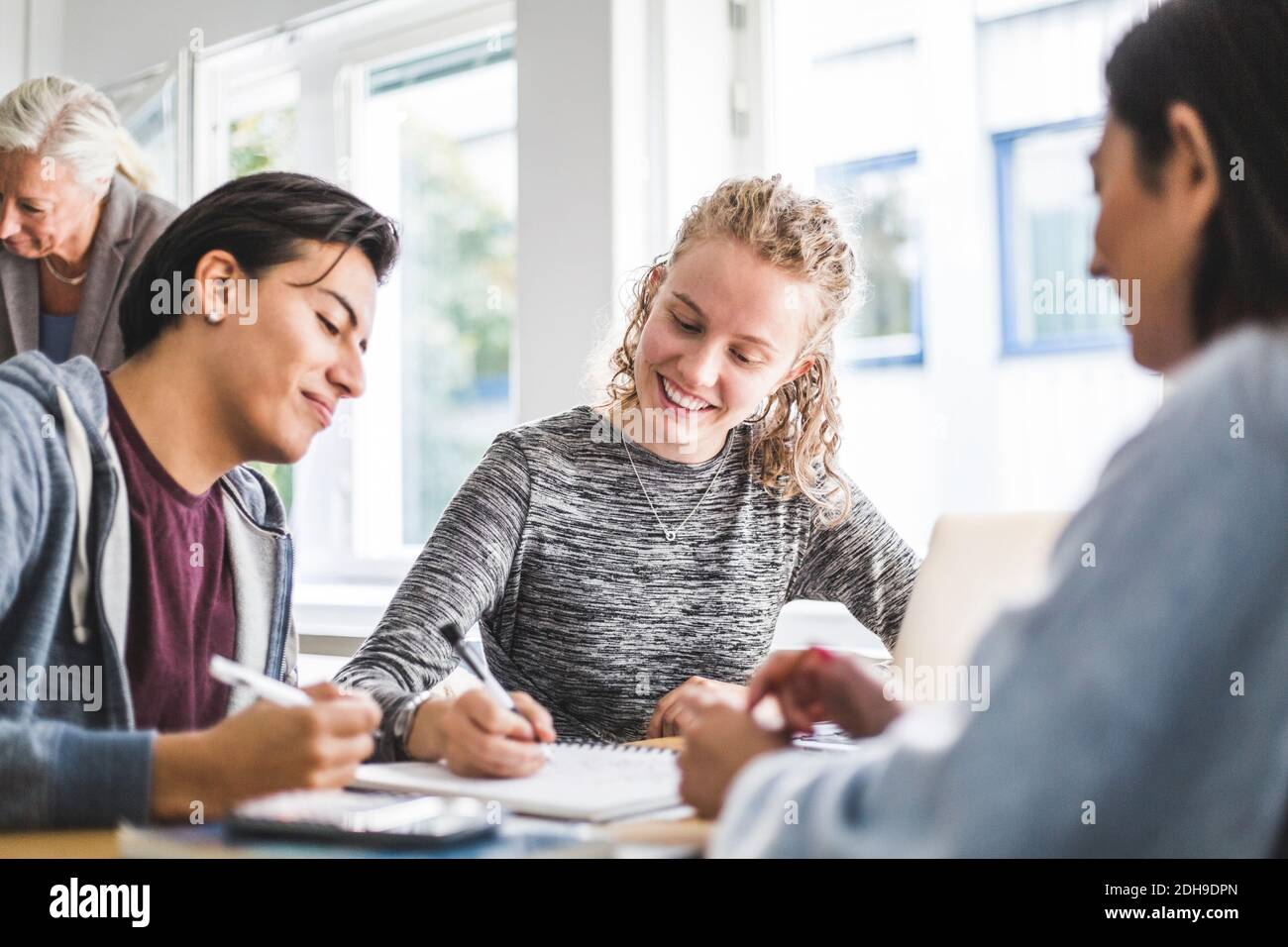 Smiling young woman discussing with male friend over book in classroom ...