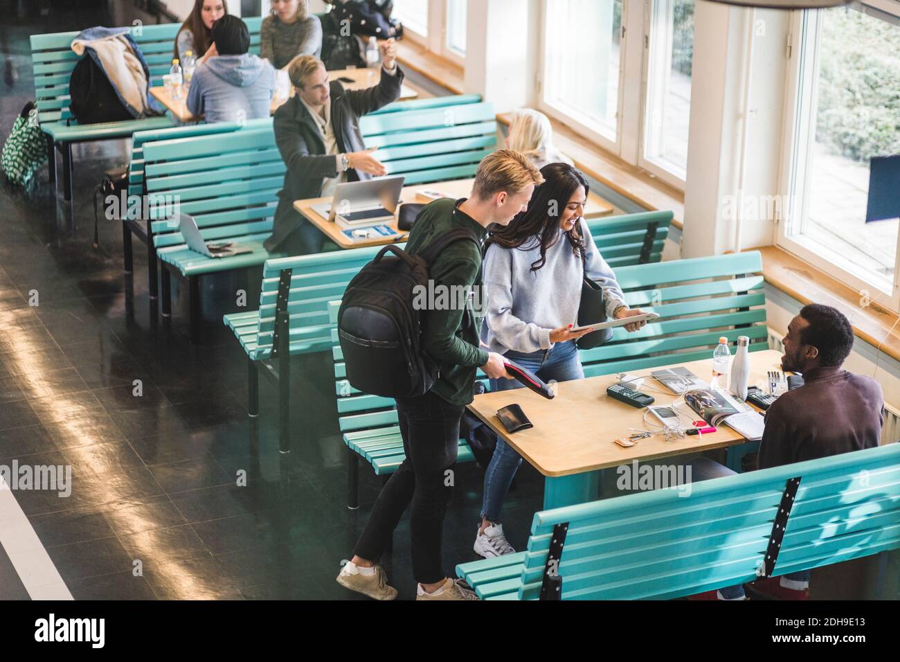 Male and female students talking with friend sitting at table in ...