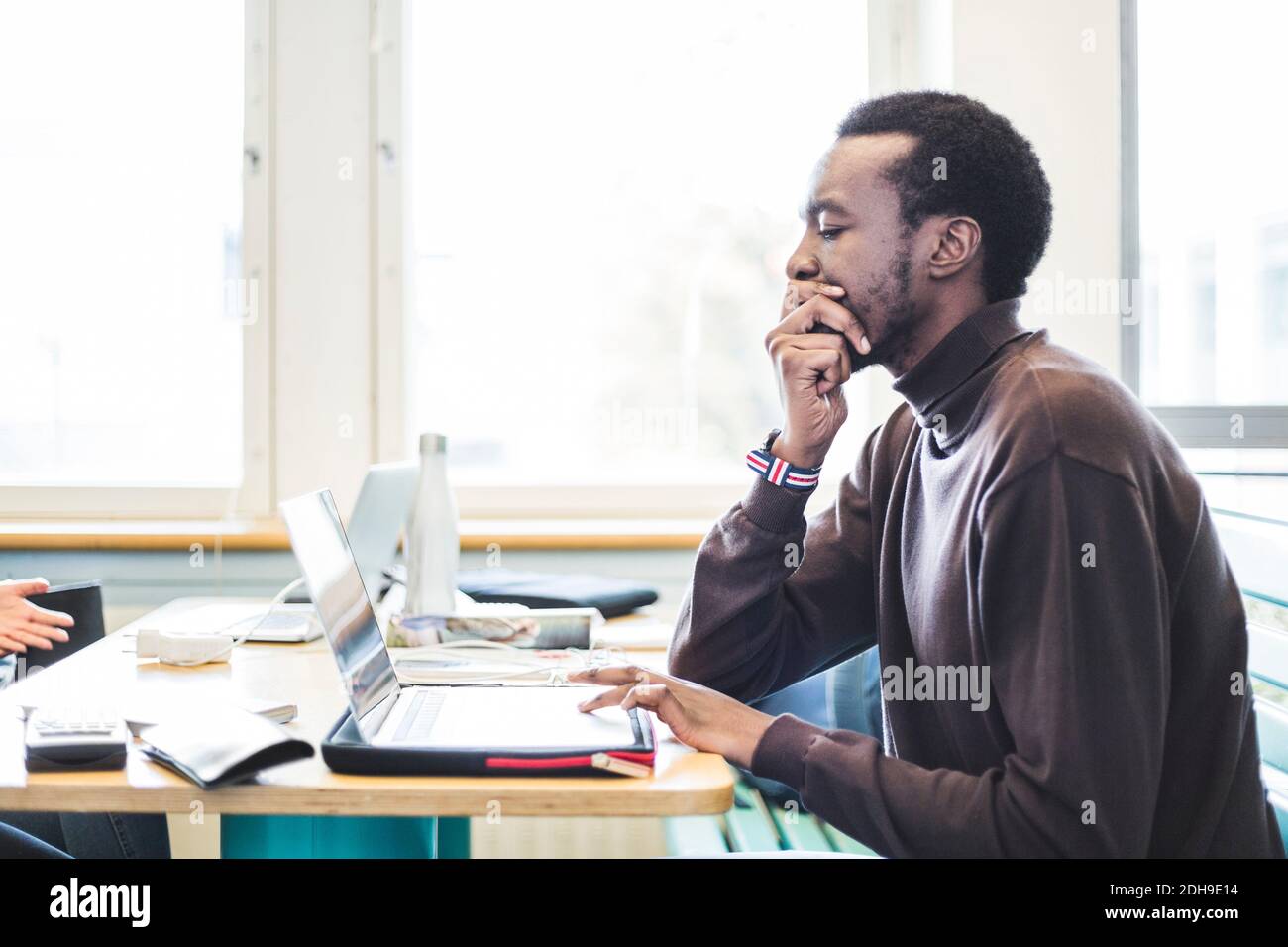 Side view of young male student using laptop at table in university ...