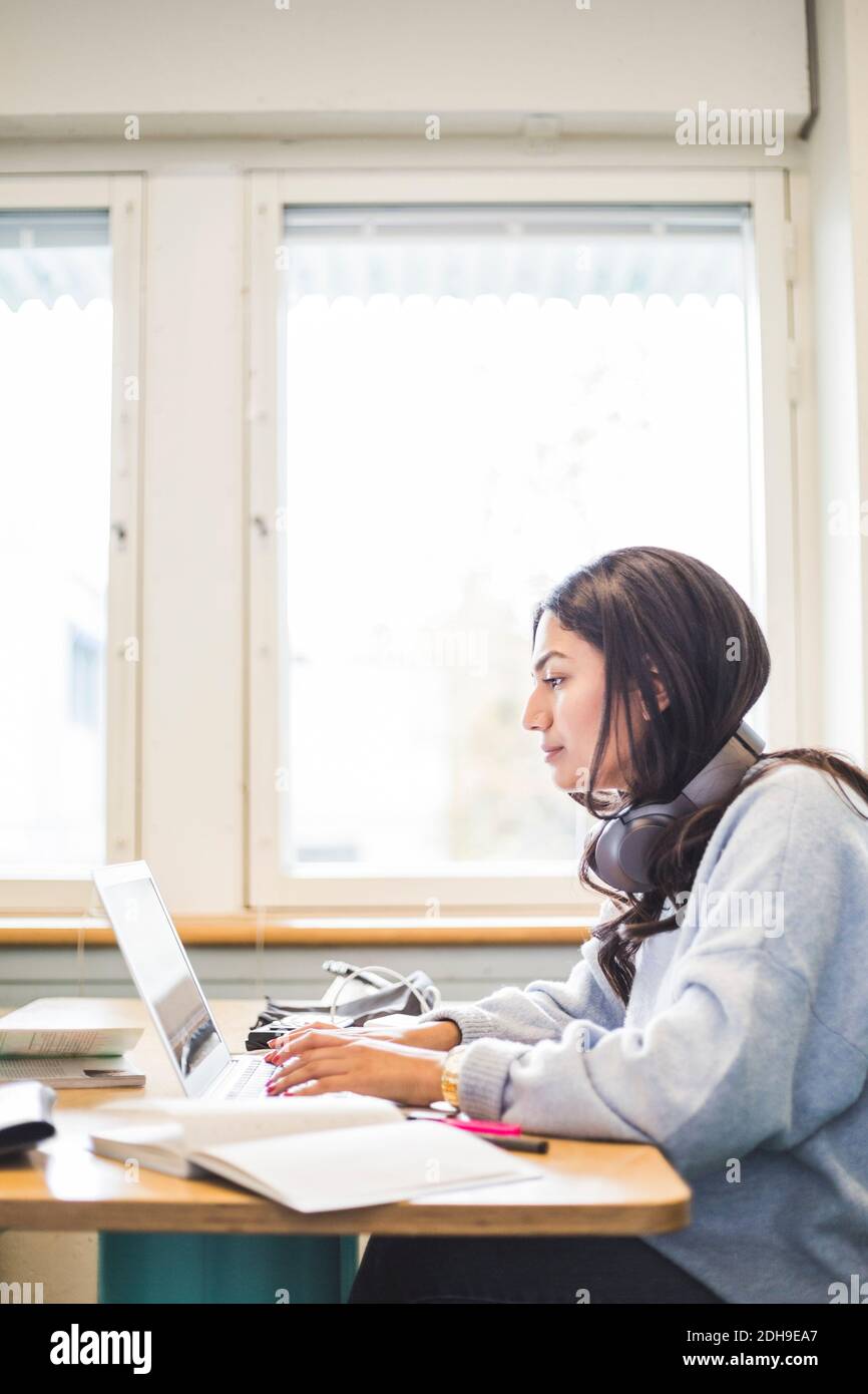 Side view of young female students using laptop in cafeteria at ...