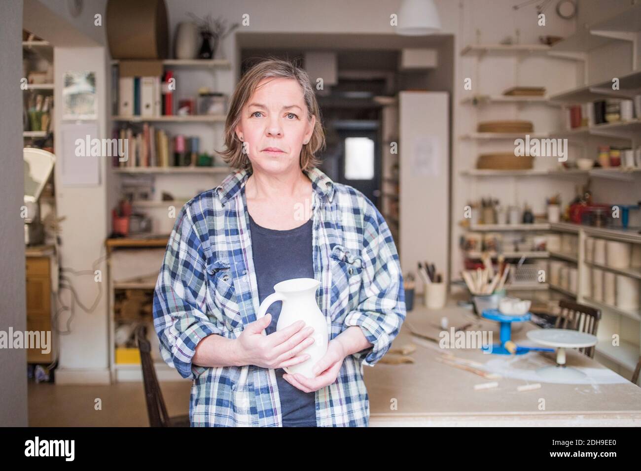 Portrait of mature female potter holding pitcher jug at workshop Stock ...
