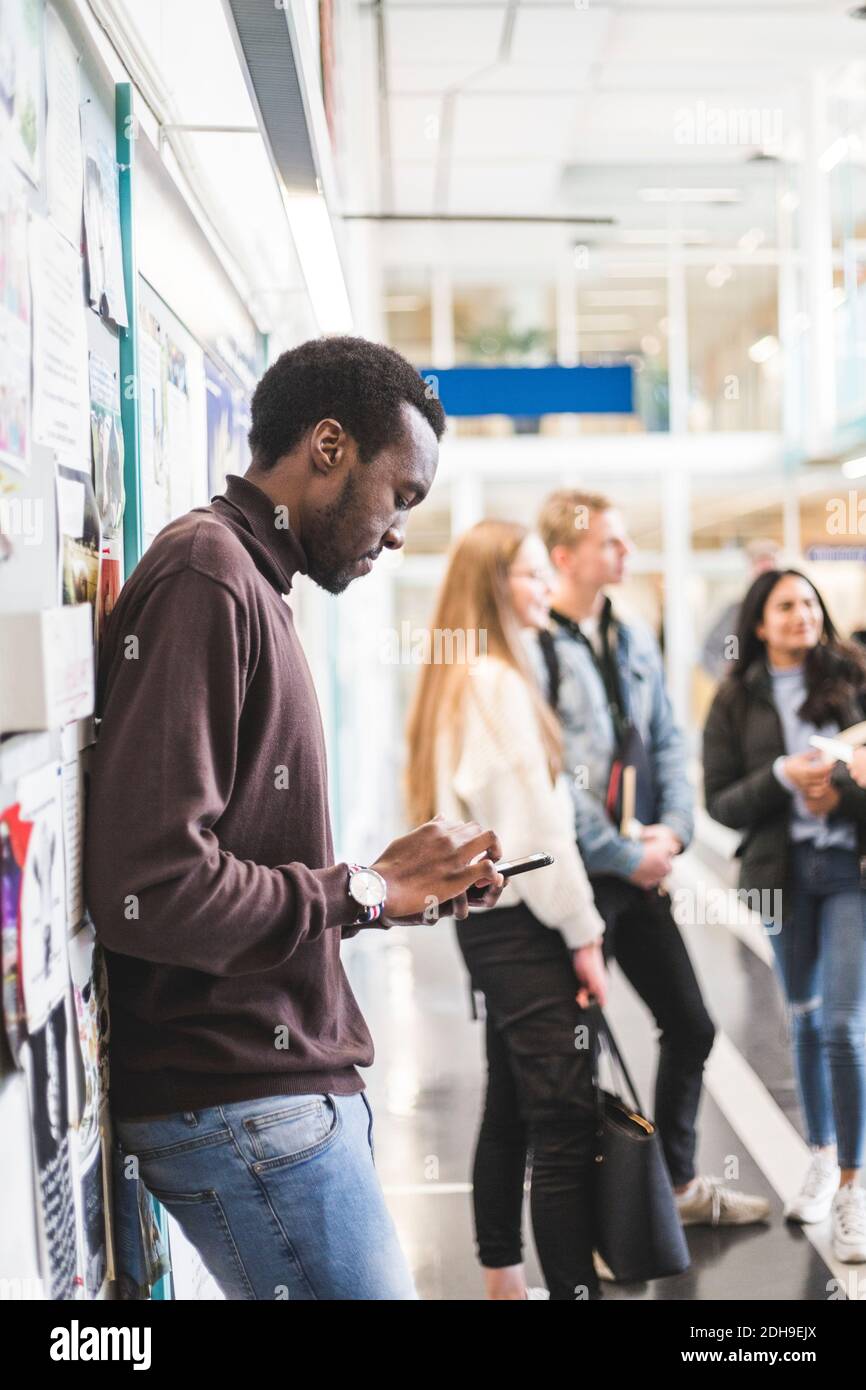 Side view of young man using mobile phone while leaning on wall at ...