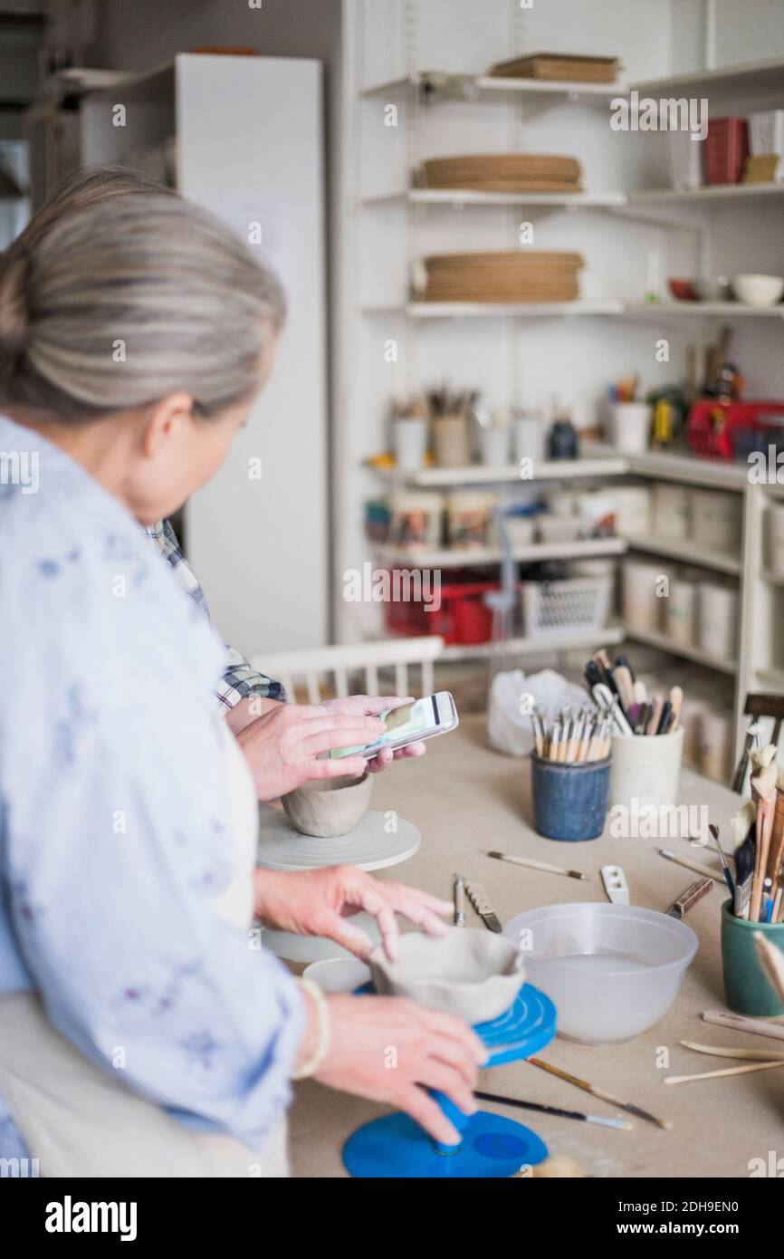 Side view of female potter showing mobile phone to senior colleague ...