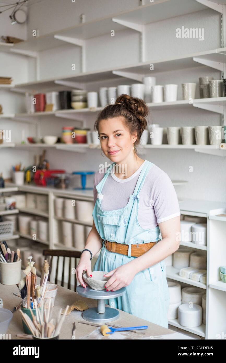 Portrait of smiling young potter molding shape on clay while standing ...