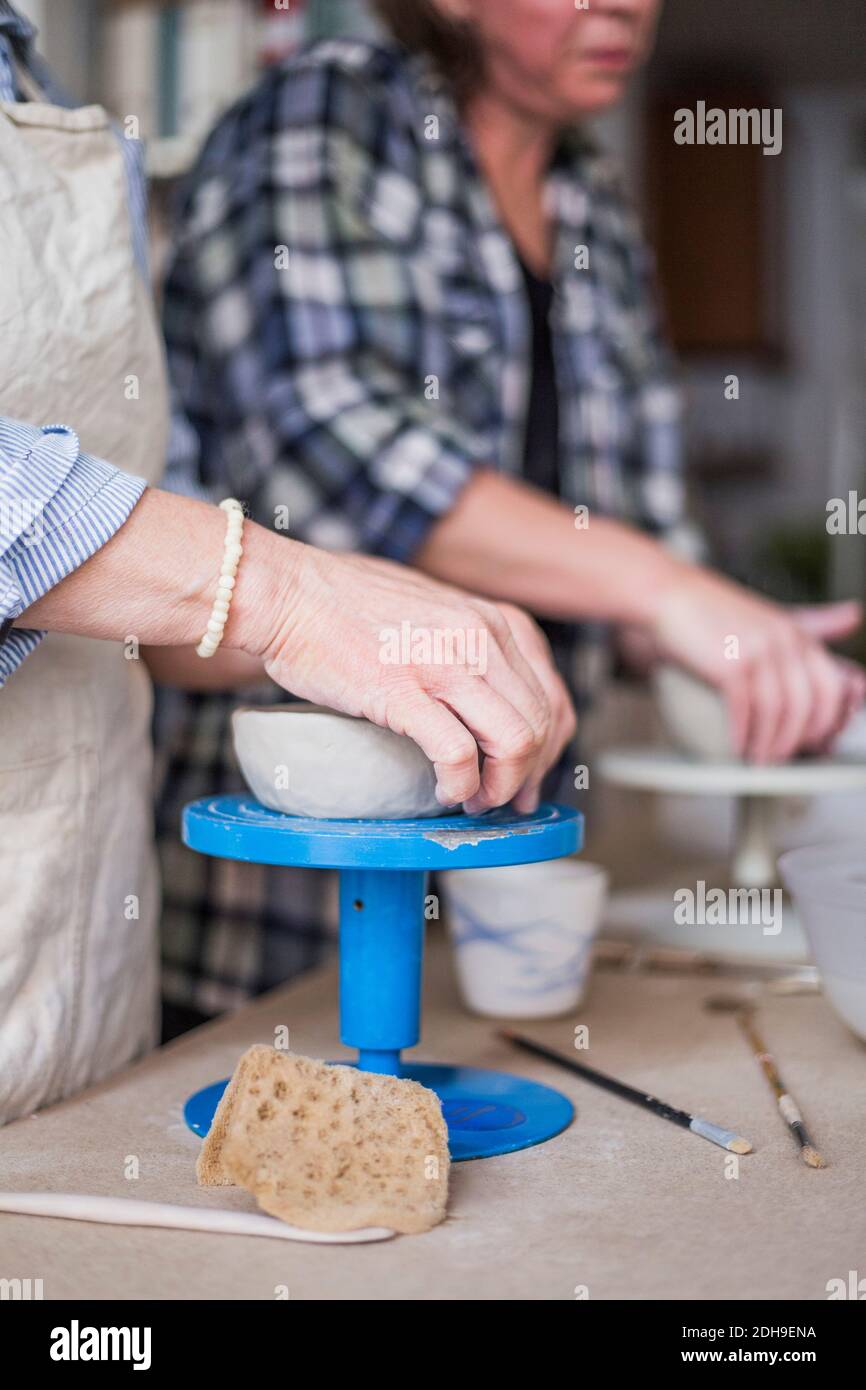 Midsection of female potters molding shape from clay at workbench in ...