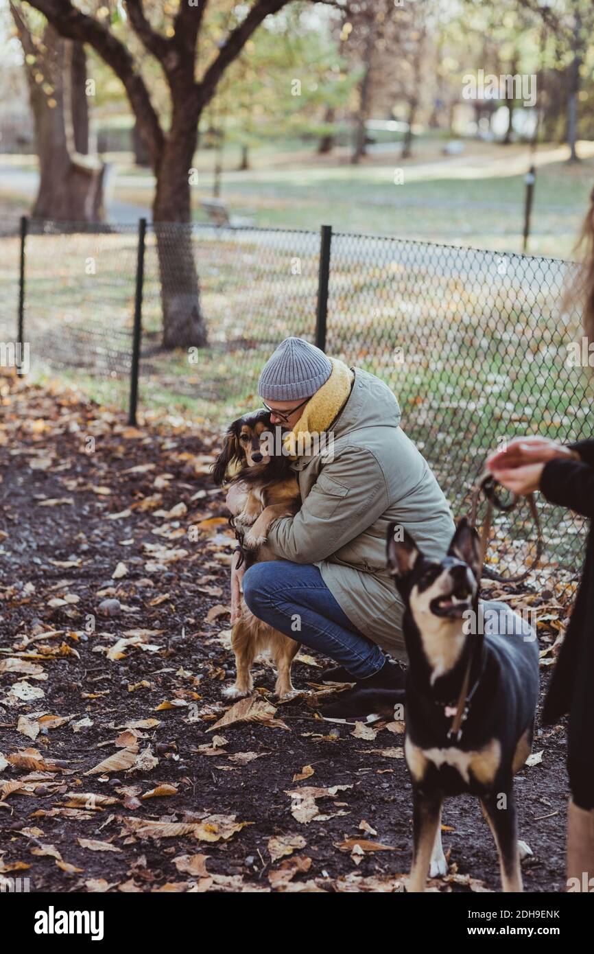Side view of man crouching while embracing dog at park Stock Photo - Alamy