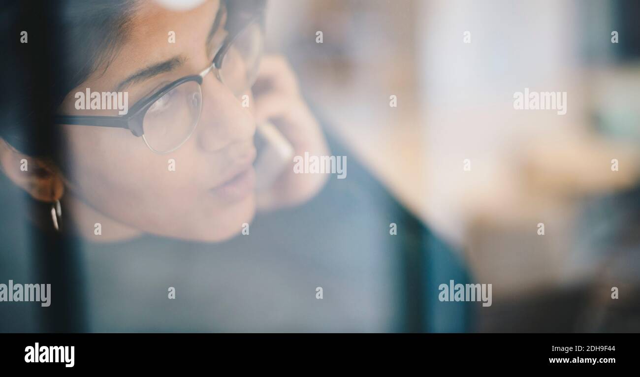 High angle view of businesswoman using smart phone seen through glass ...