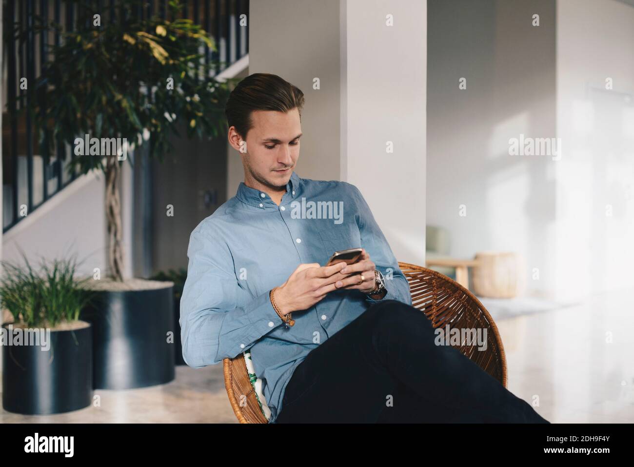 Businessman using smart phone while sitting on chair in office Stock ...