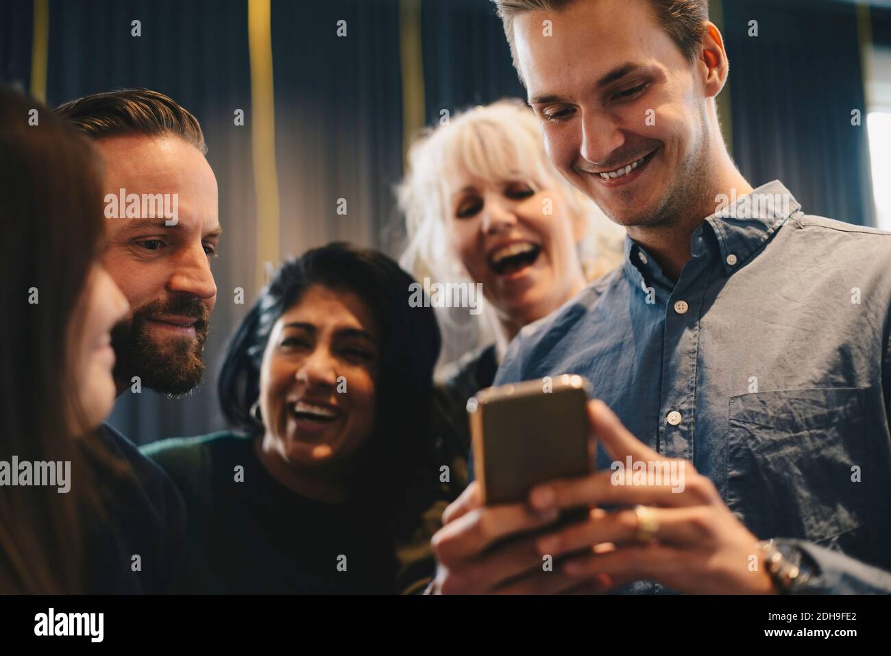 Happy business people using smart phone with male colleague in office ...