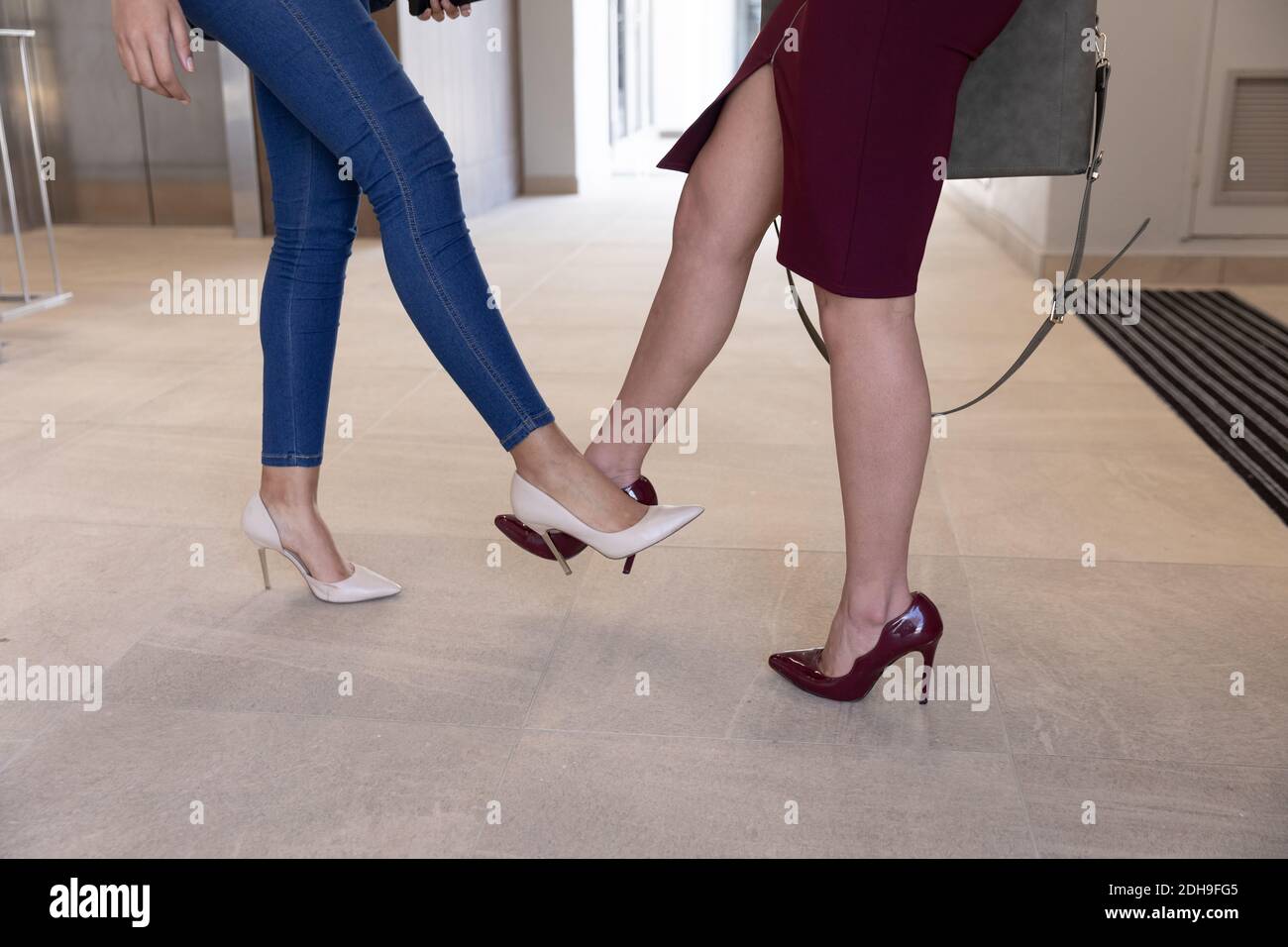 Low section of two businesswomen greeting each other by touching feet ...