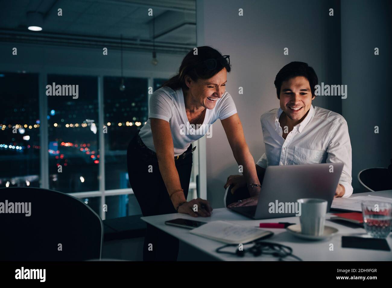 Smiling male and female colleagues discussing over laptop while working ...