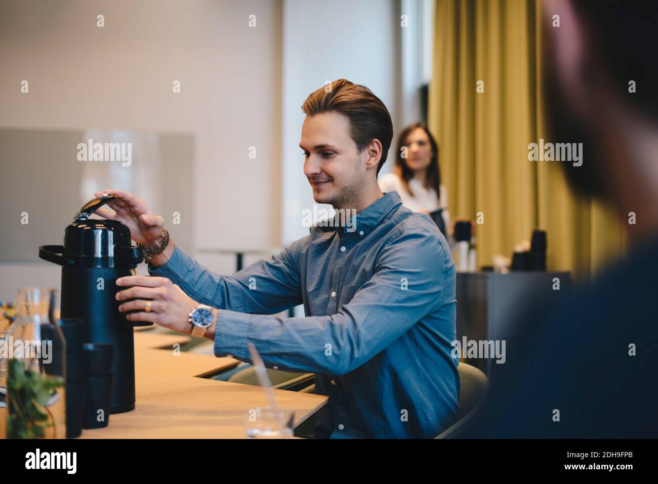 Smiling businessman opening insulated drink container at conference ...