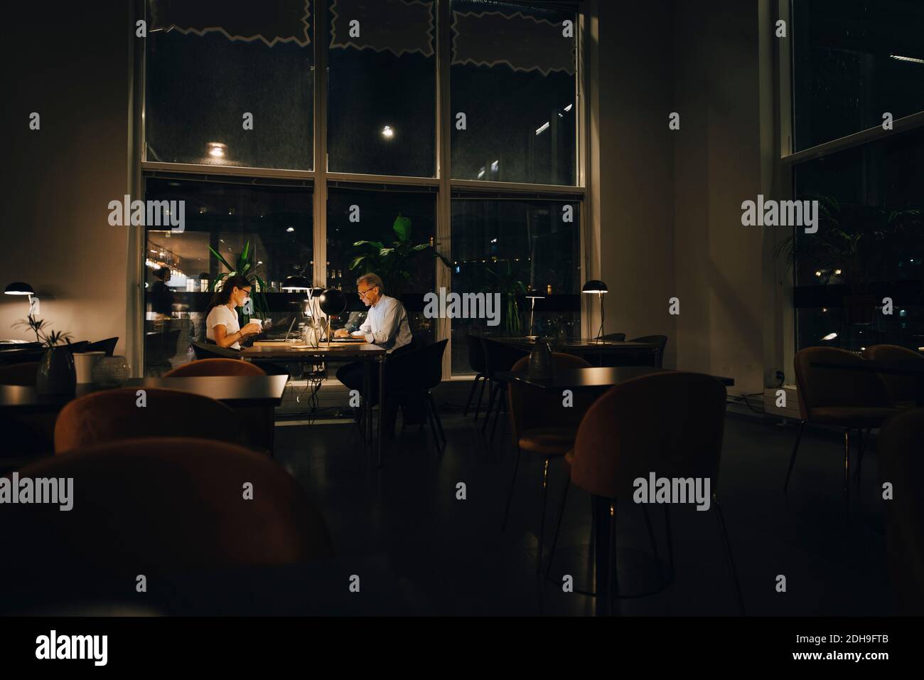 Male and female entrepreneurs working late in dark office at night ...