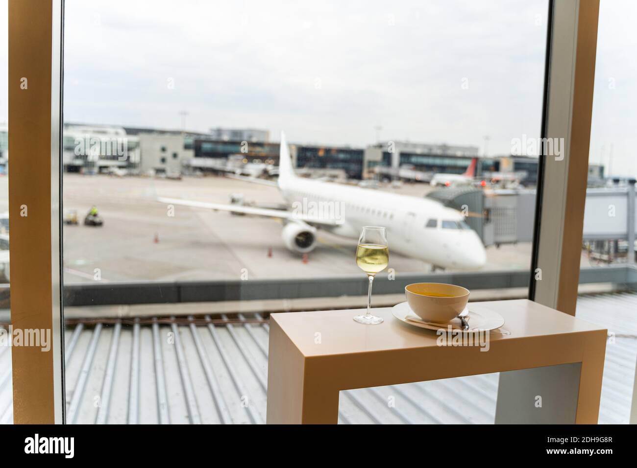 Glass of wine, bowl of soup near window with a view to airplane in ...