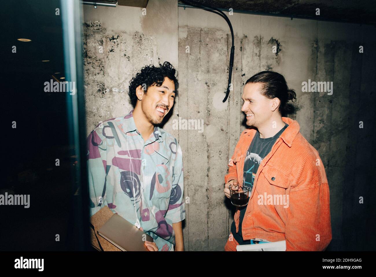 Smiling businessman and colleague talking against wall while standing ...