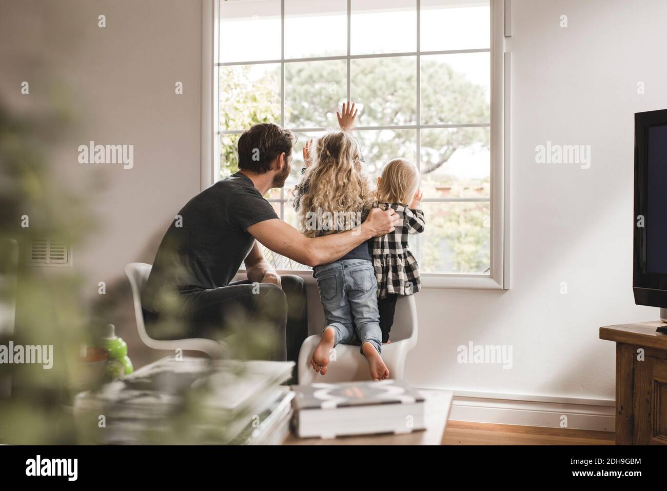 Father with daughters looking through window at home Stock Photo - Alamy