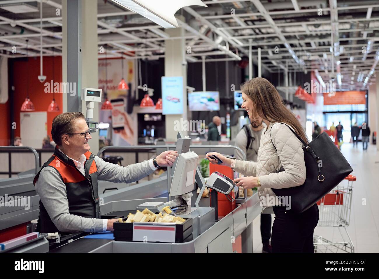 Mature cashier talking to woman while paying at checkout counter in ...