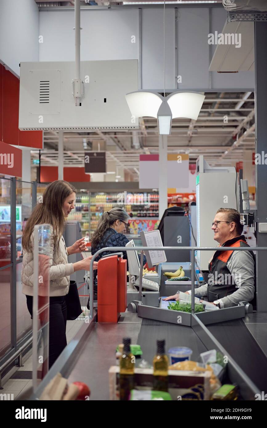 Woman talking to mature cashier while paying at checkout counter in ...
